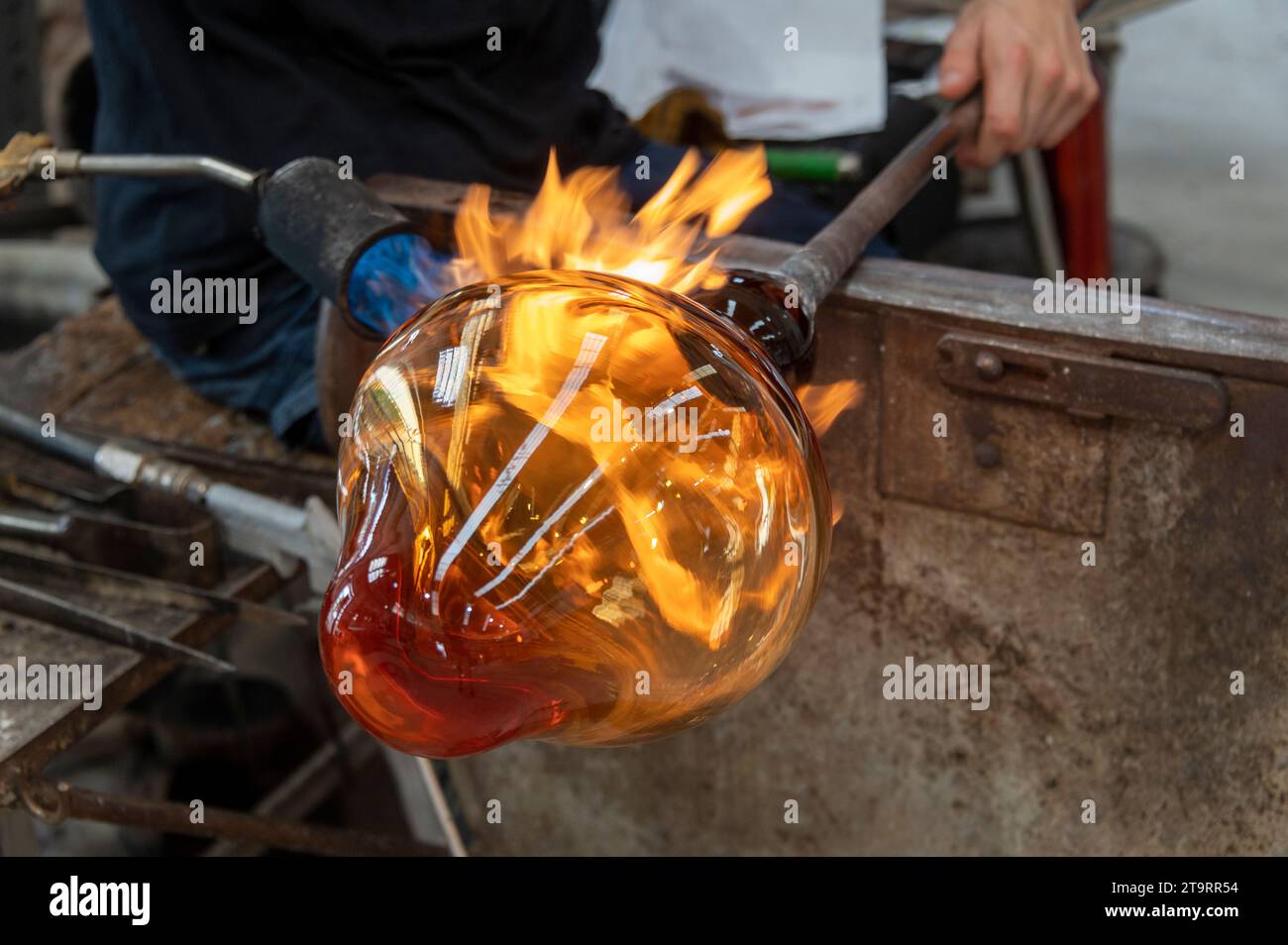 A glass vase taking shape by a glass blower using a flame torch at the ...
