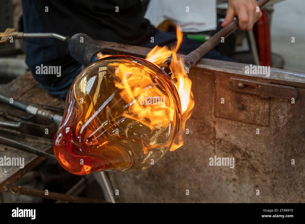 A glass vase taking shape by a glass blower using a flame torch at the ...
