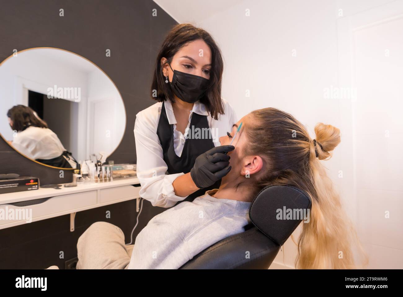 Professional brushing the eyebrows of a client sitting on a chair ...