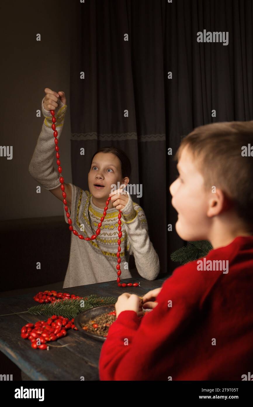 Children make garlands with their own hands. Red rosehip garlands using ...