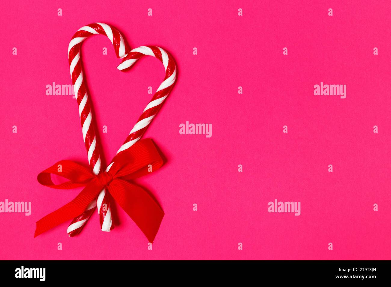 Two Christmas candy canes overlapping to form a heart and a red bow on ...