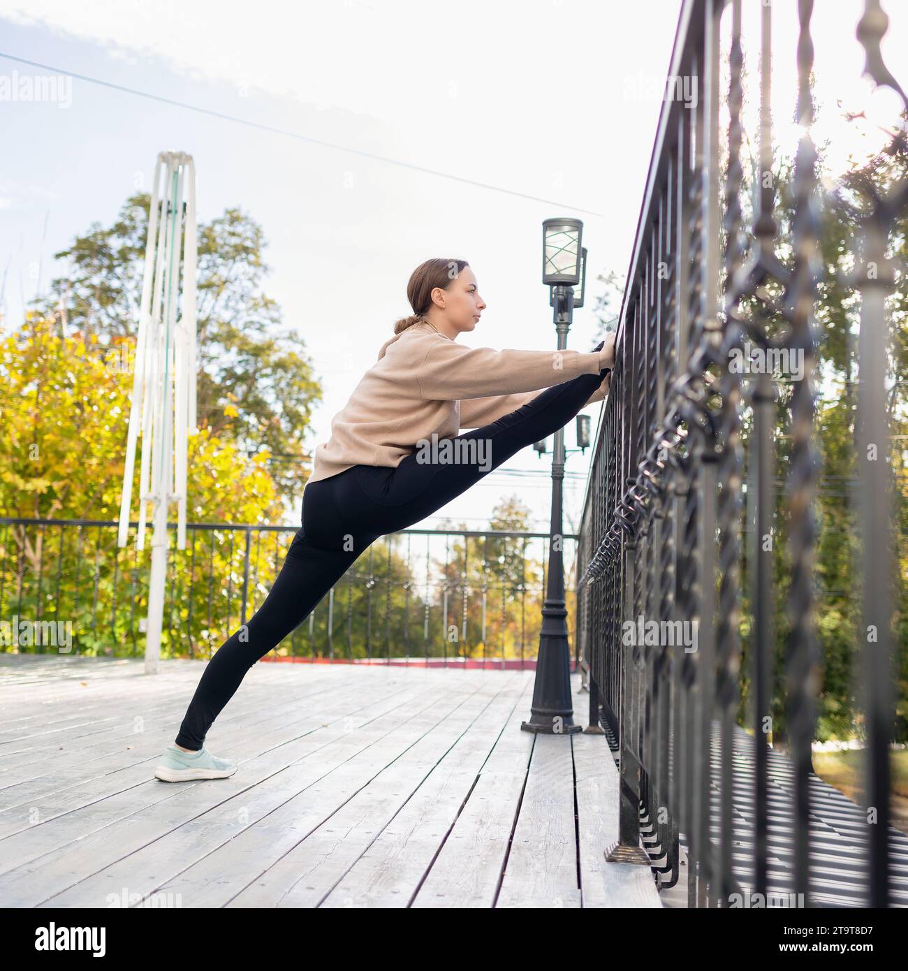 A young woman performs an exercise to stretch the muscles of her legs ...