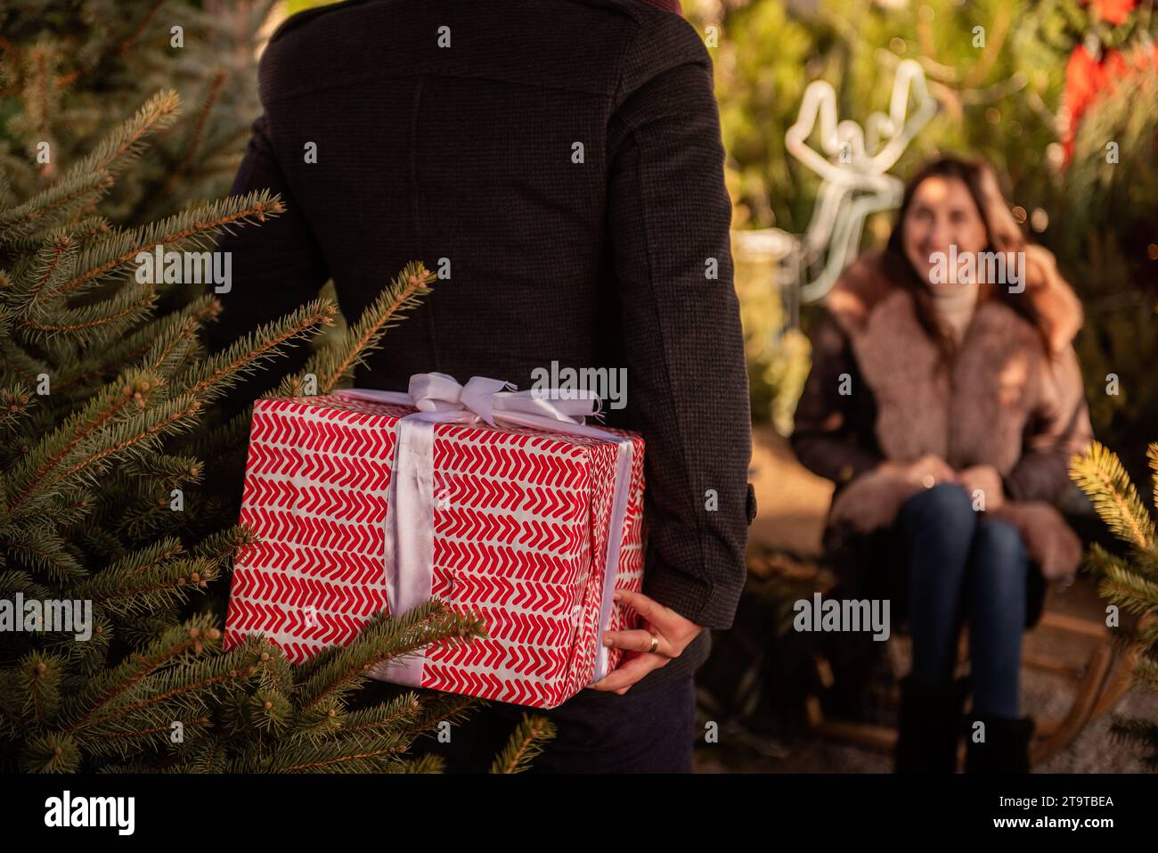 Young man holds large red box behind his back. Beautiful woman covers ...