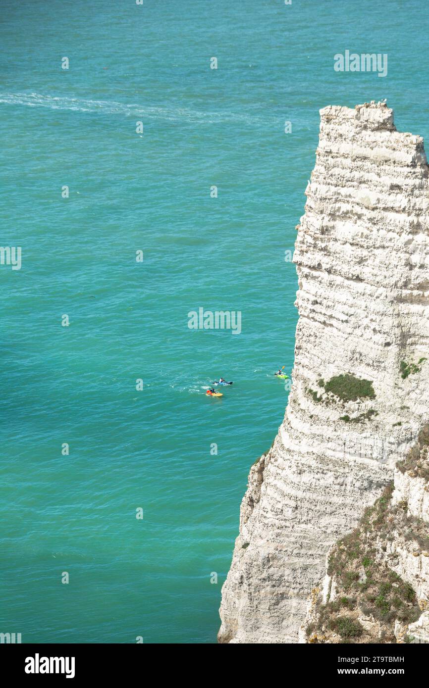 A white towering sea cliff stand out from sapphire blue sea with people ...