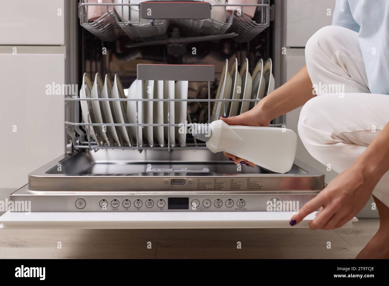 female hand pours rinse aid into the dishwasher compartment in modern ...