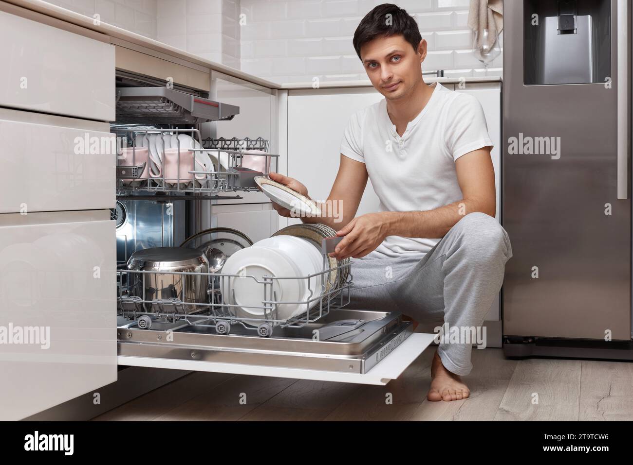 handsome positive man pulls out clean dishes from the dishwasher in ...
