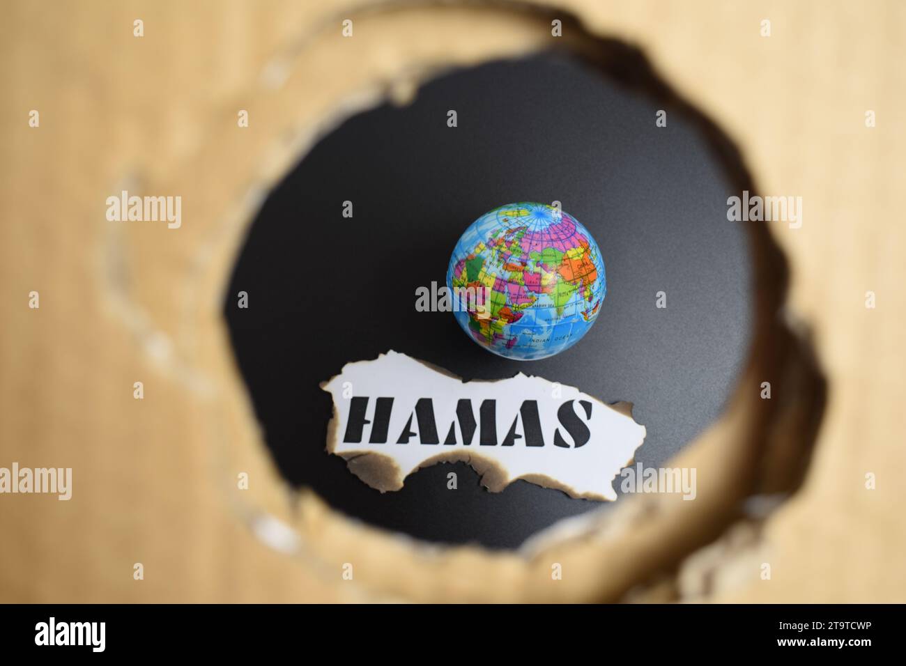 View through the hole. The word Hamas written on burnt paper, globe on ...