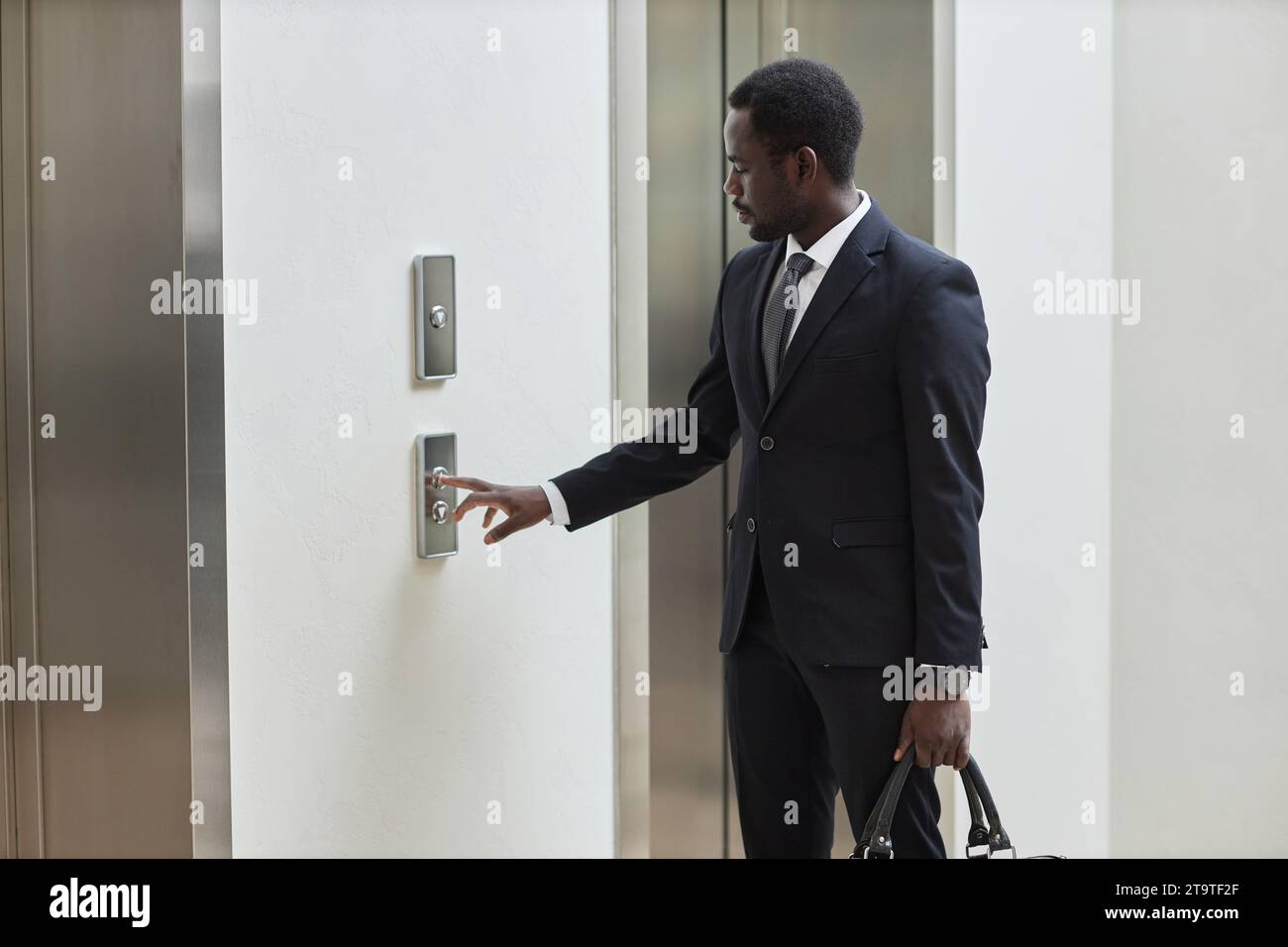 Medium long shot of Black man dressed in business suit calling elevator ...