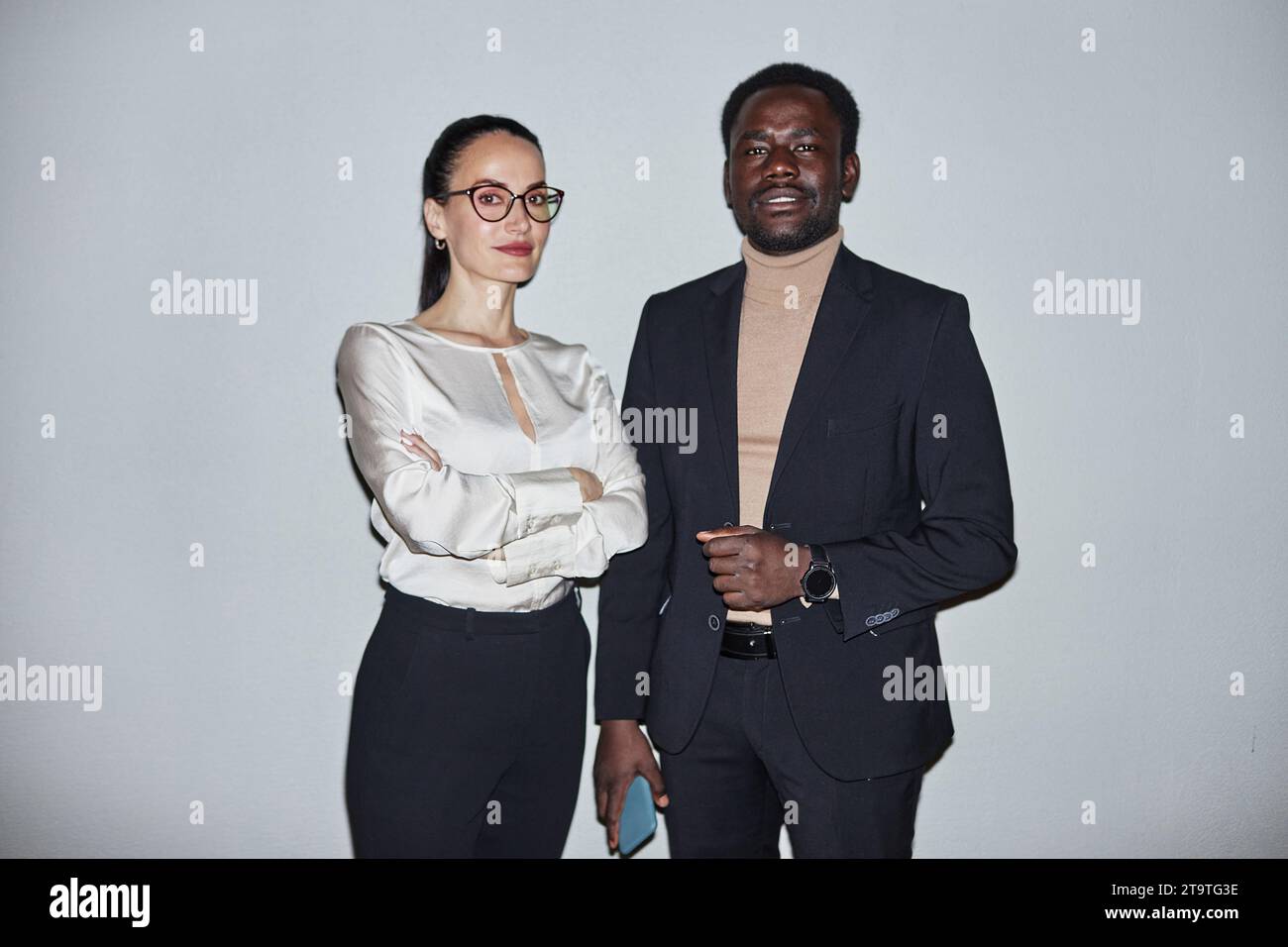 Two happy diverse corporate employees standing against light background ...