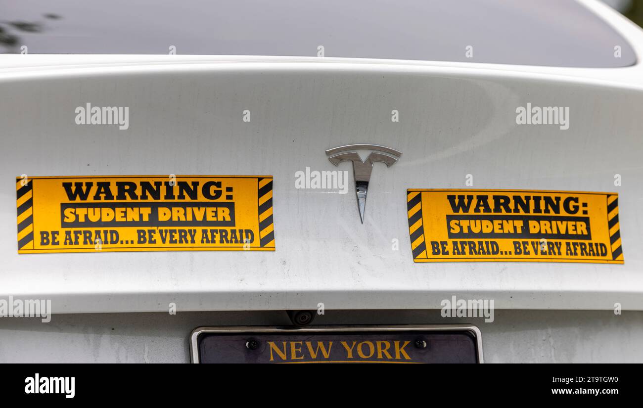 two bright stickers on the back of a white telsa stating student driver ...