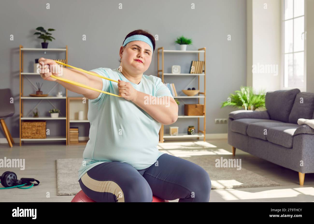 Fat funny woman doing stretching exercises with rubber band sitting on ...