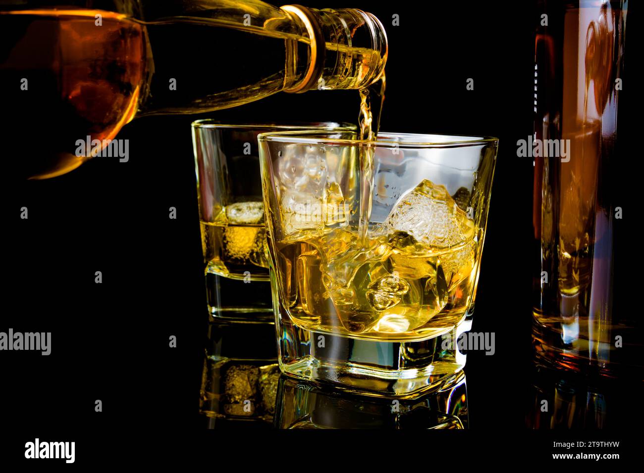 barman pouring whiskey in front of whiskey glass and bottles on black ...