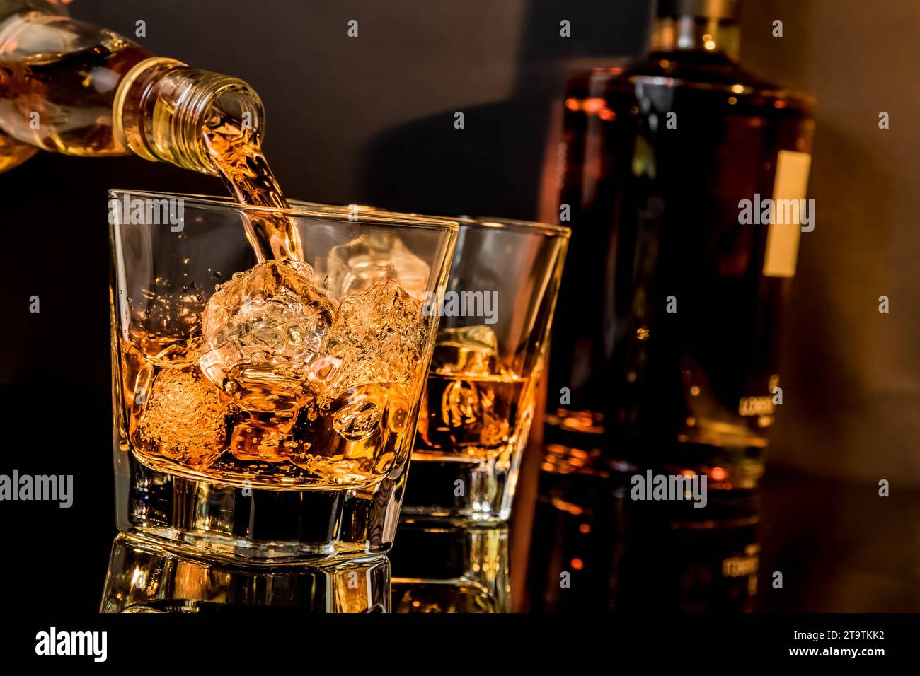 barman pouring whiskey in front of whiskey glass and bottles on black ...