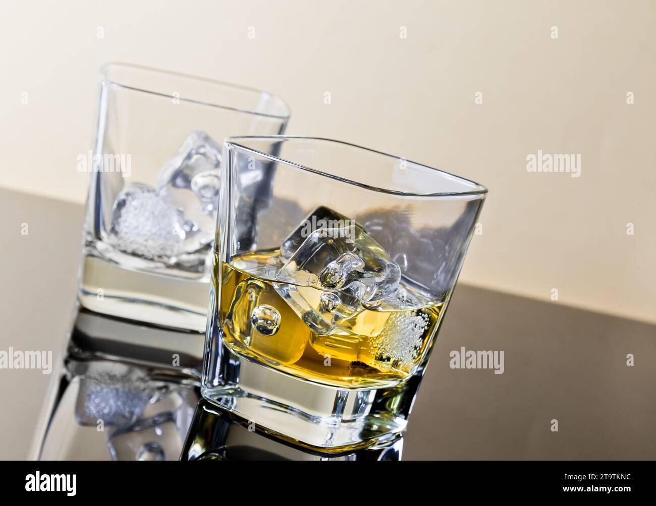 one glass of whiskey and one empty with ice cubes on black table with ...