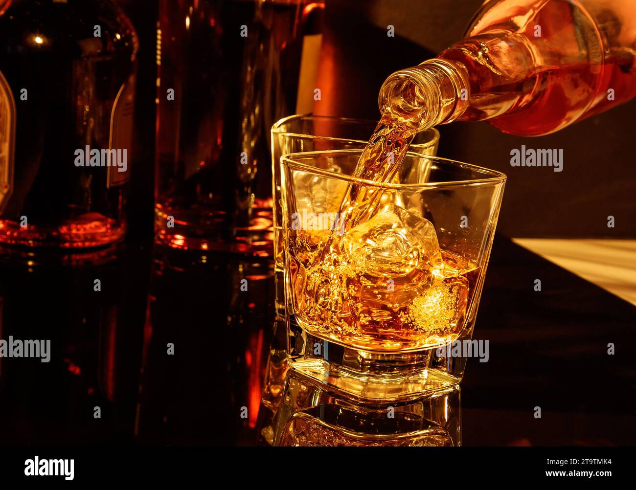 barman pouring whiskey in front of whisky glass and bottles on black ...