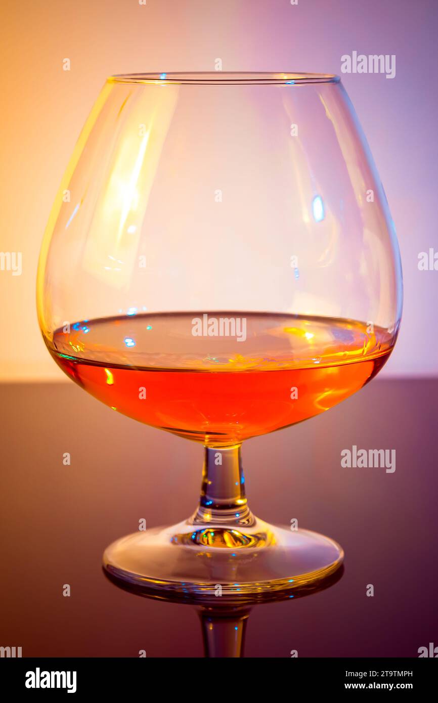 snifter of brandy in elegant typical cognac glass on colored light ...