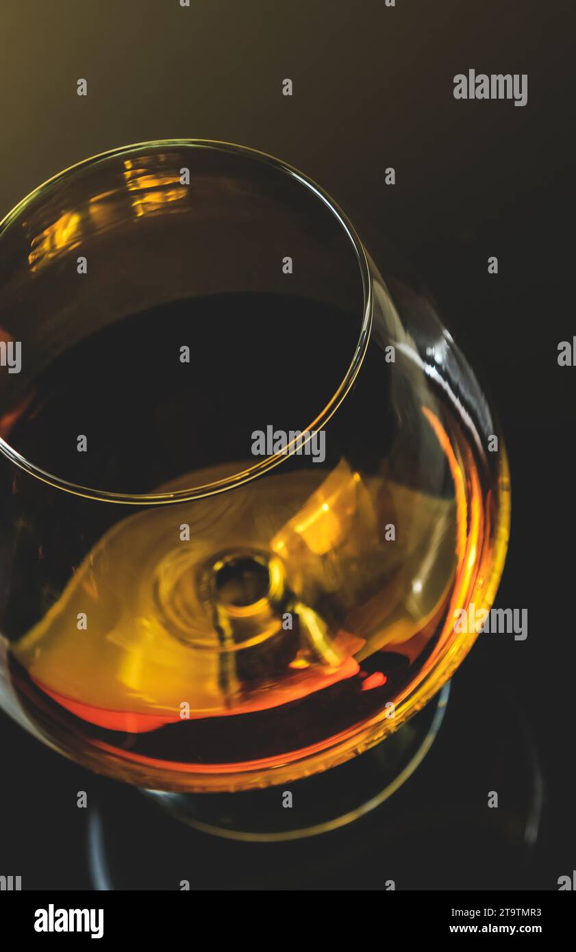 top of view of snifter of brandy in elegant typical cognac glass on dark background with golden ...