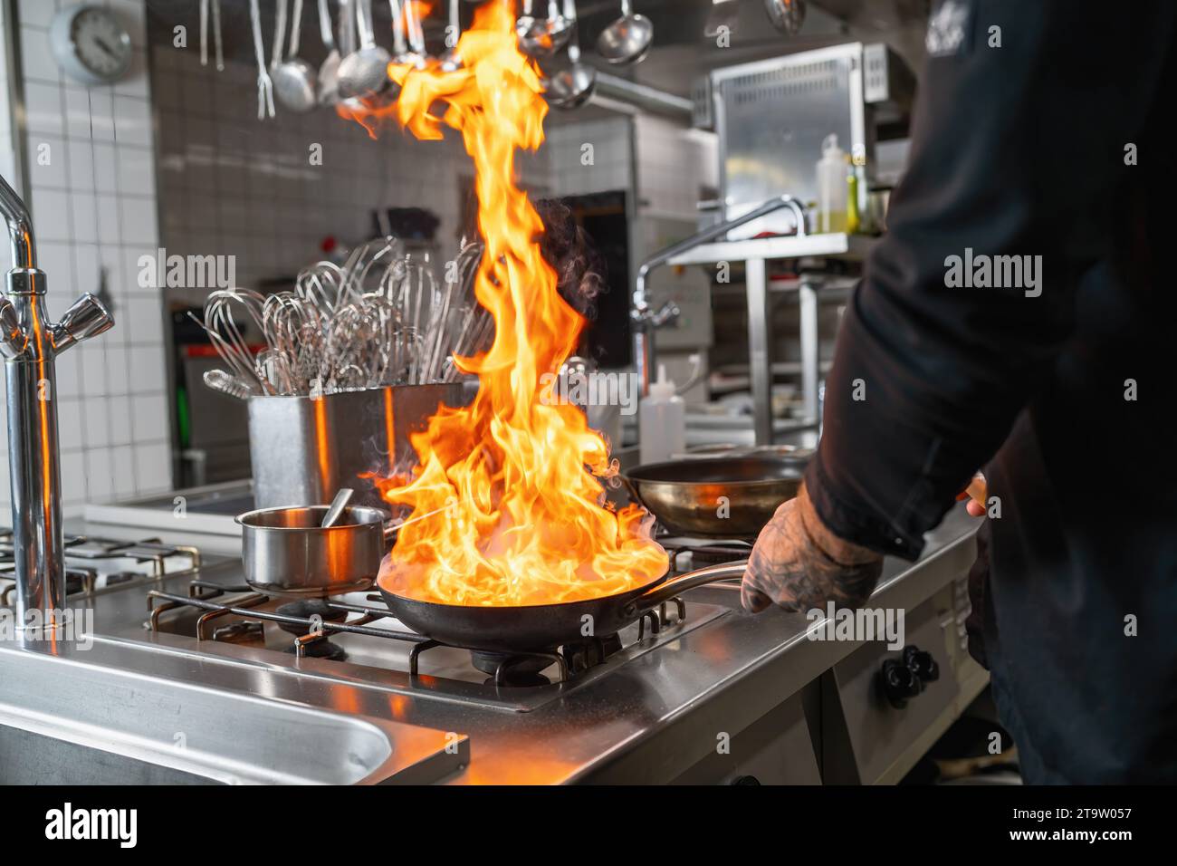 Pro chef flambeing in the kitchen in a pan on a gas-fired stove. Luxury ...
