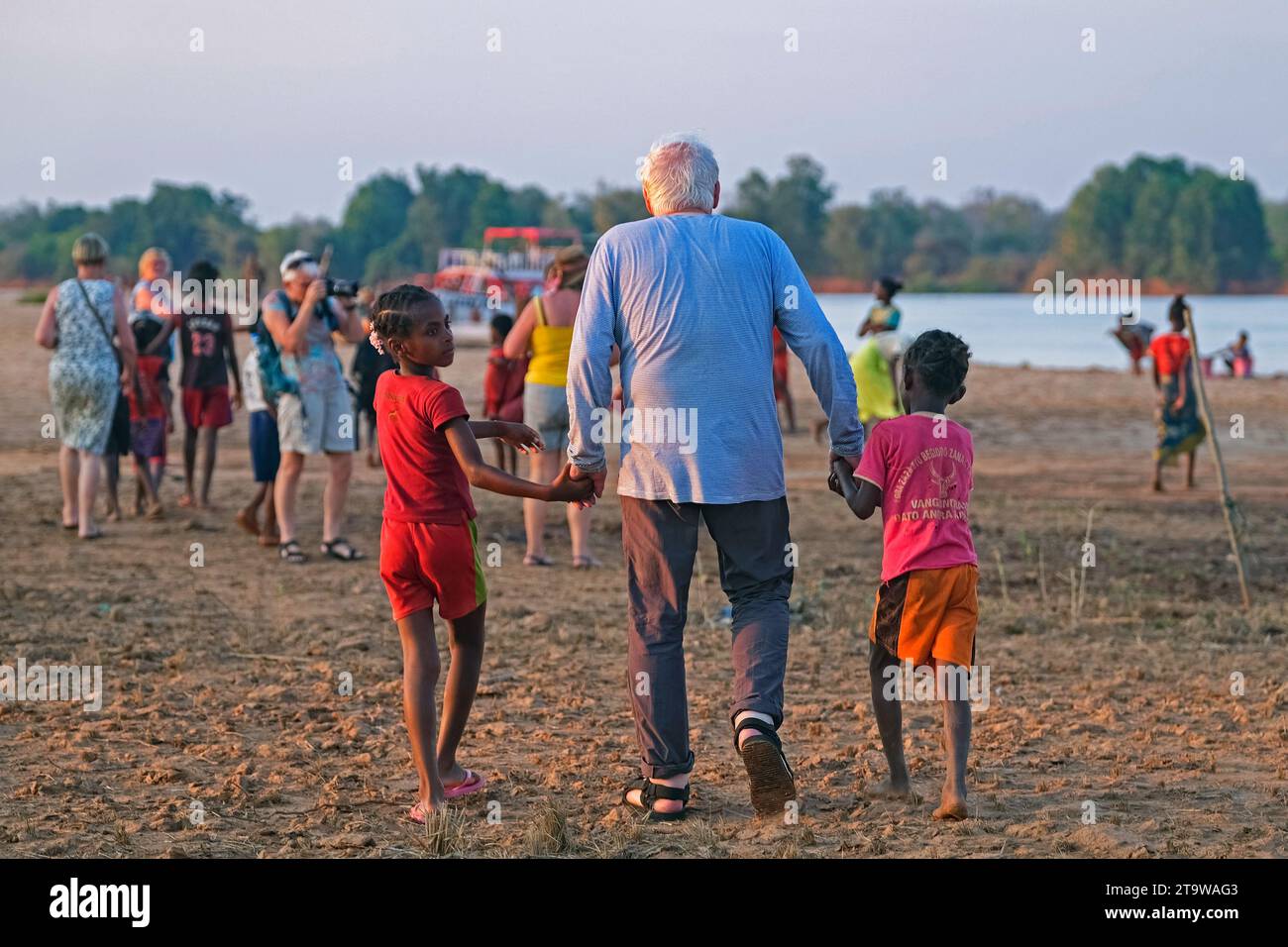 Malagasy children helping elderly Western tourist walking back to boat ...