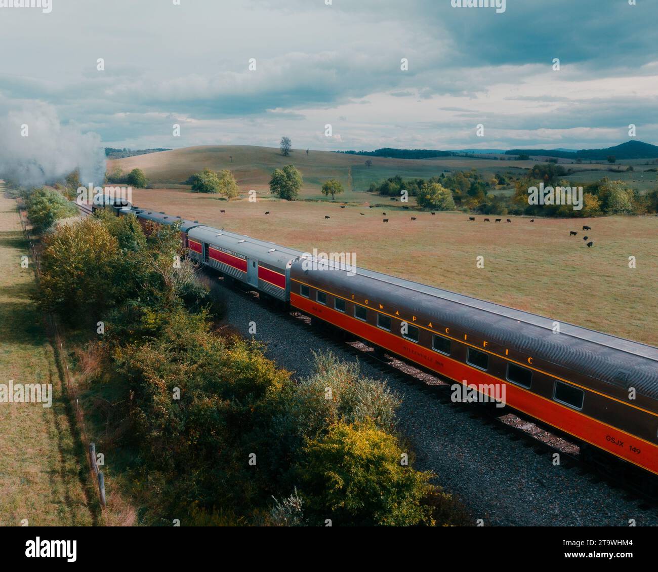 A long locomotive train is slowly chugging past a scenic landscape of ...