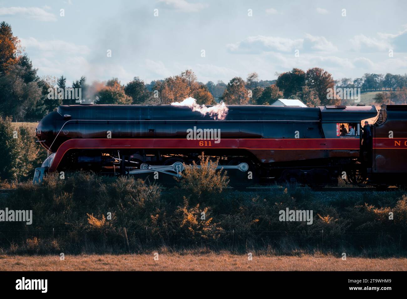 A vintage-style black and red steam locomotive and passenger cars ...