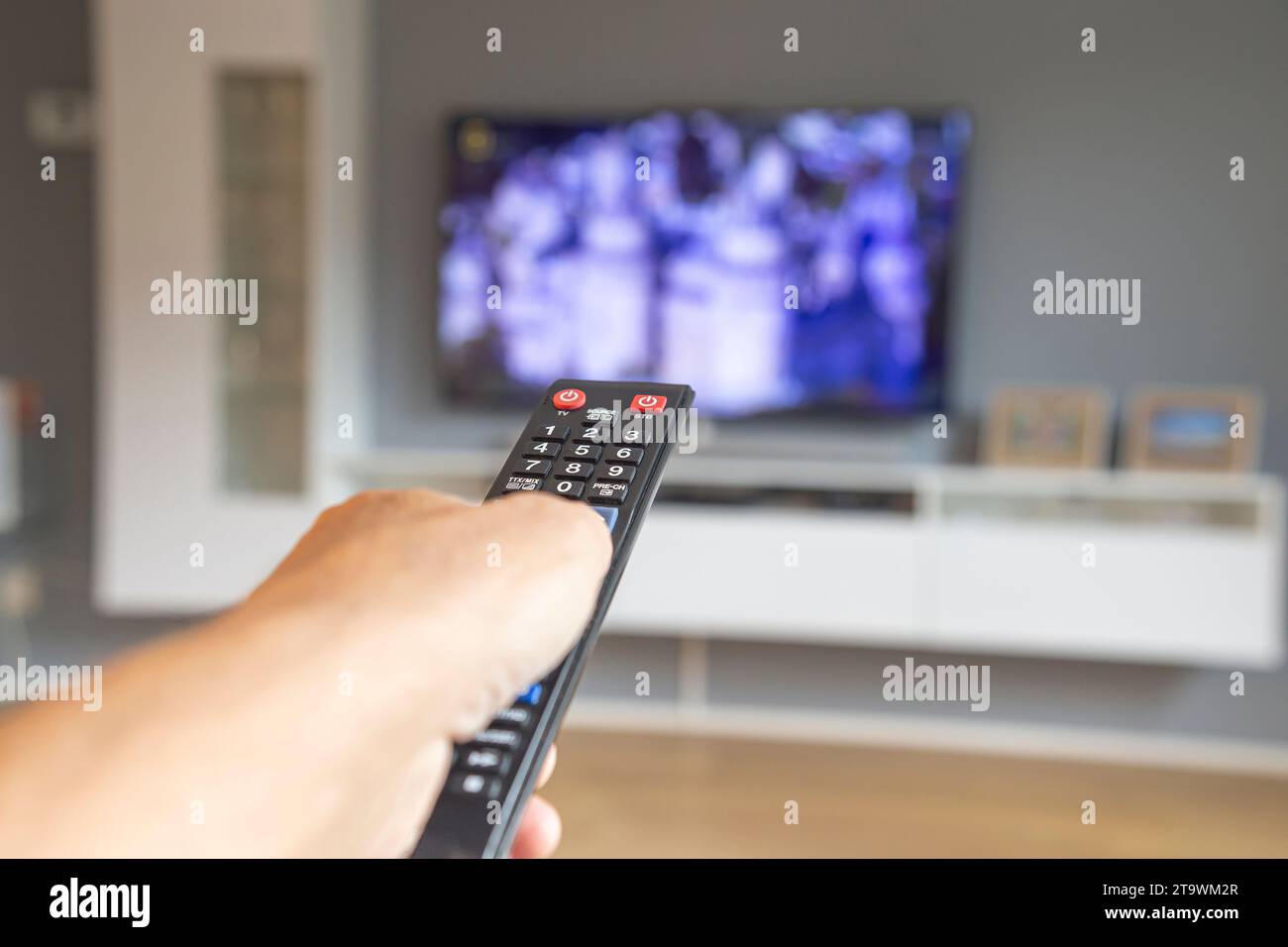 Closeup to a male hand holding a black TV controler with a blurred flat ...