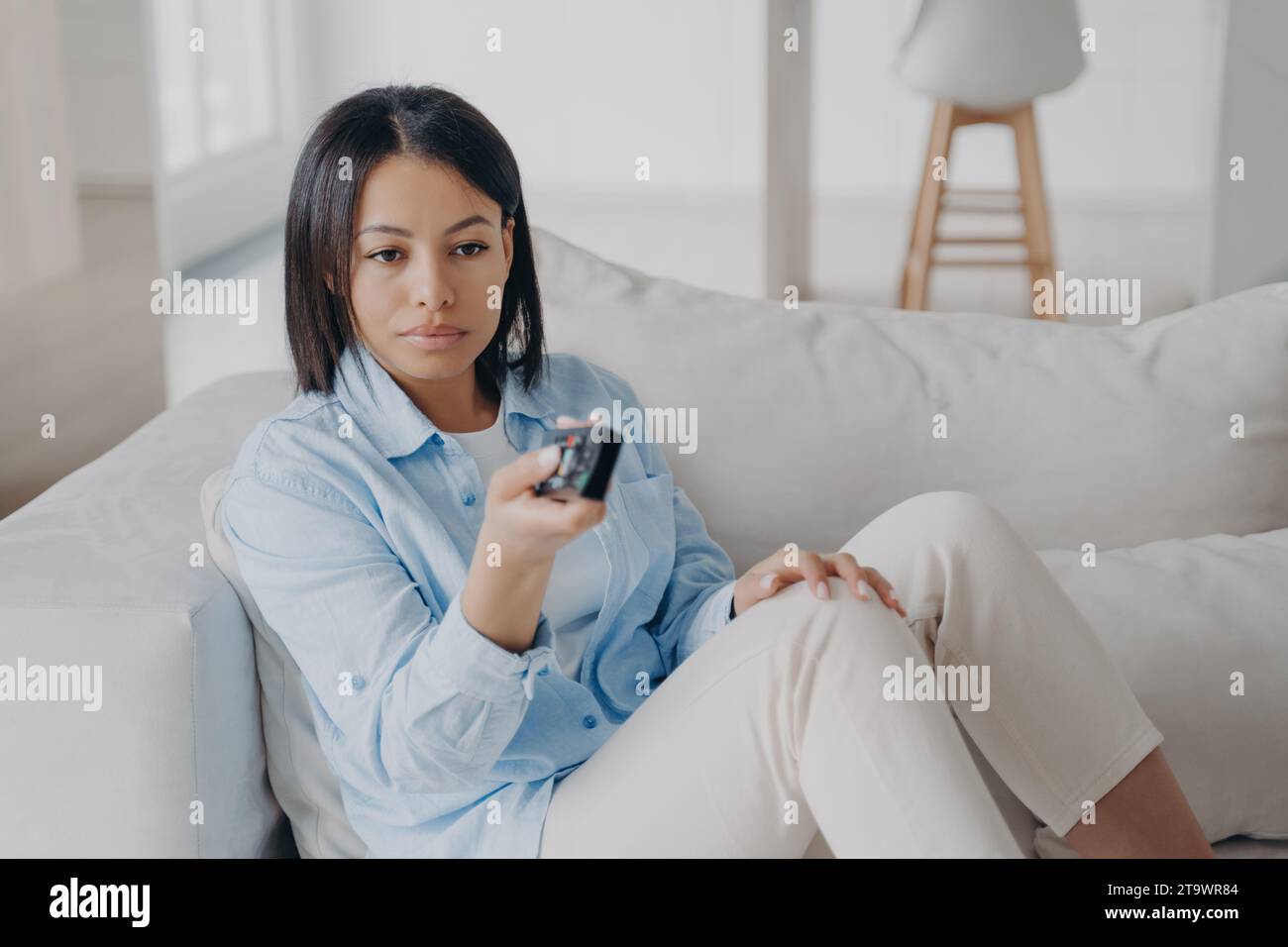 Serene young woman with remote control, choosing from various ...