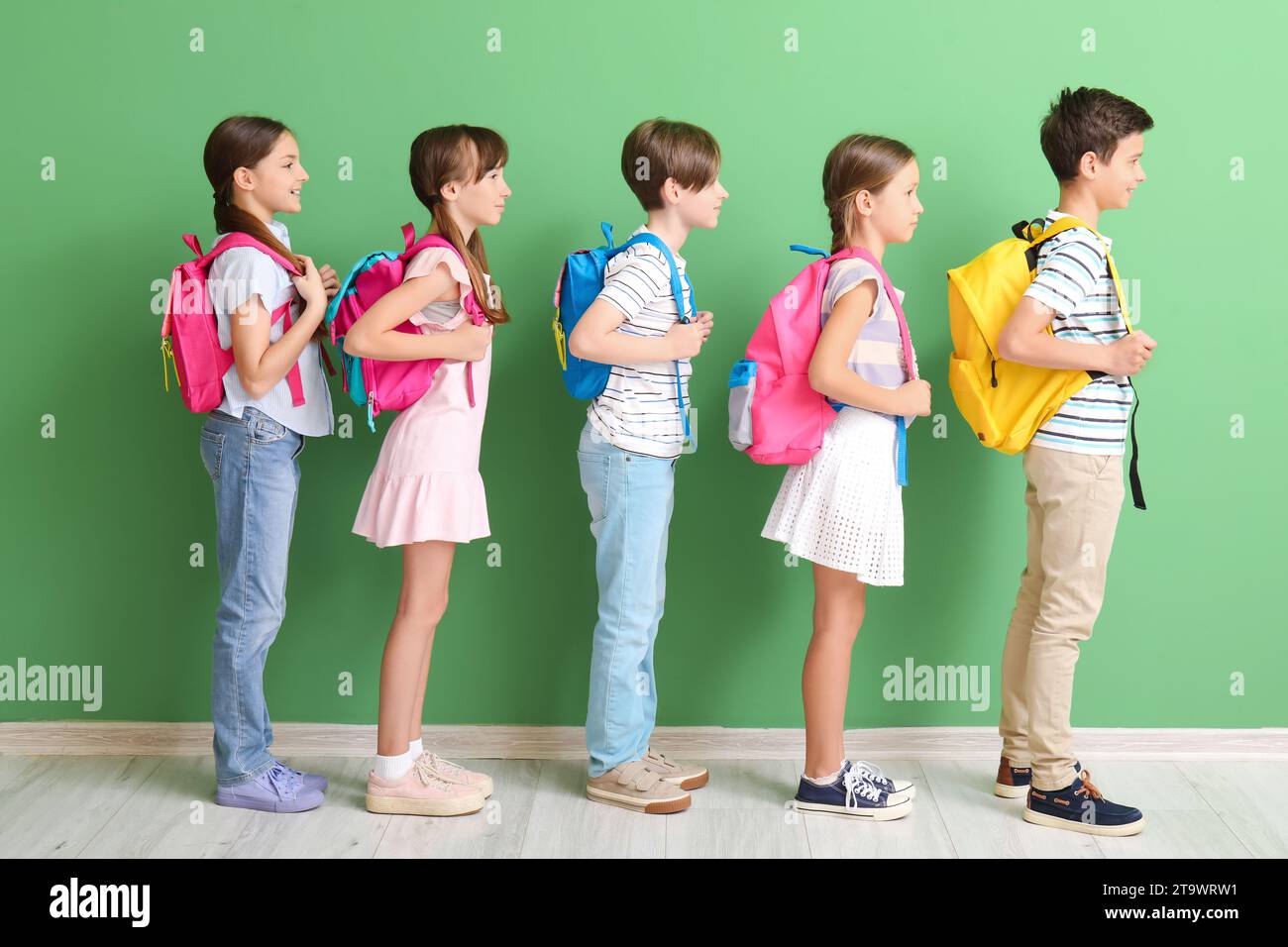 Little pupils with backpacks near green wall Stock Photo - Alamy