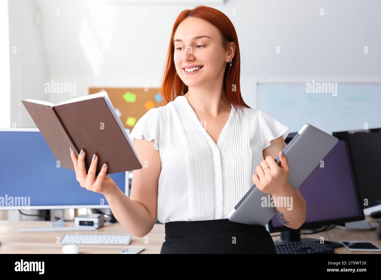 Female teacher with book and laptop at school computer lab Stock Photo ...