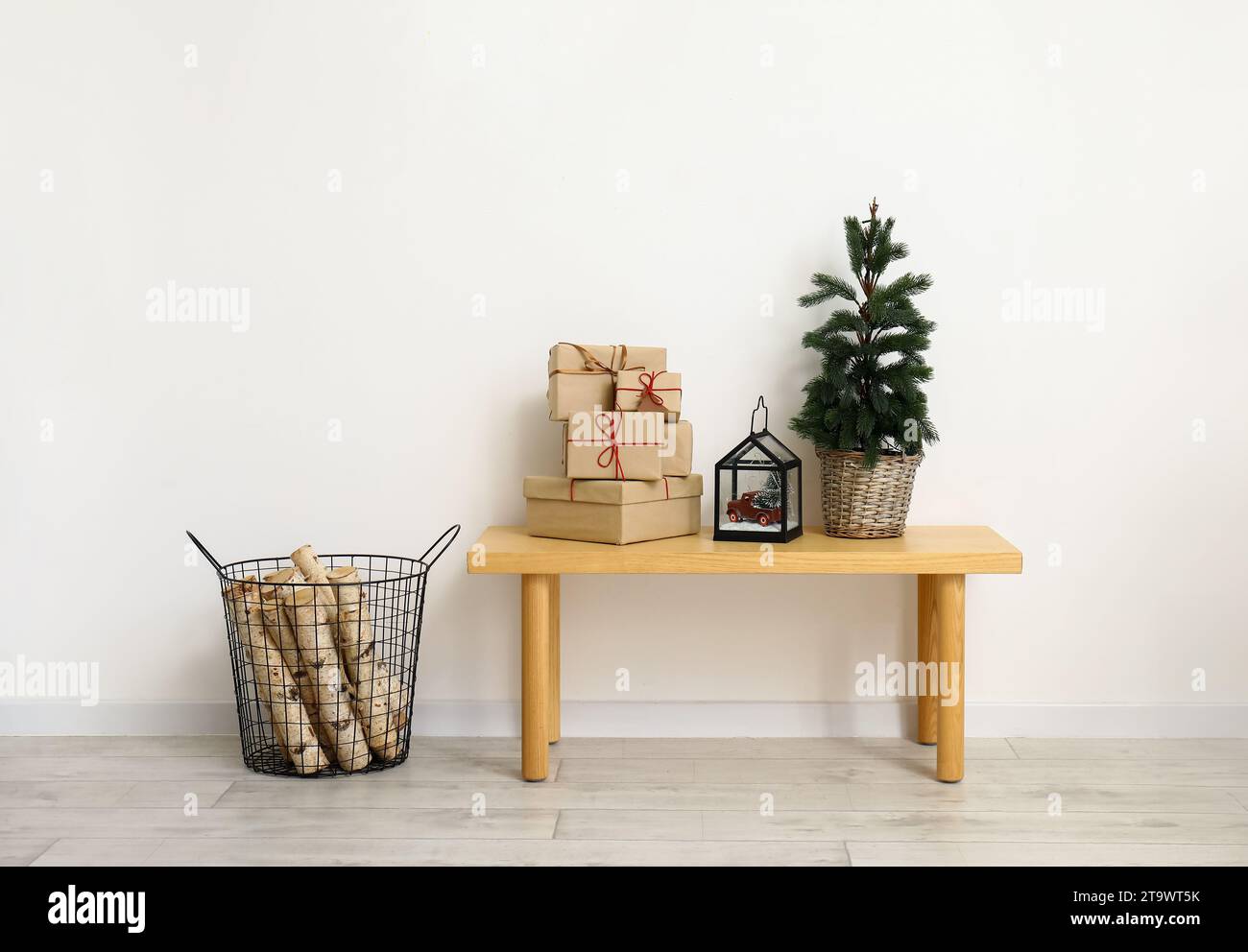 Bench with Christmas tree, gift boxes and firewood near white wall ...