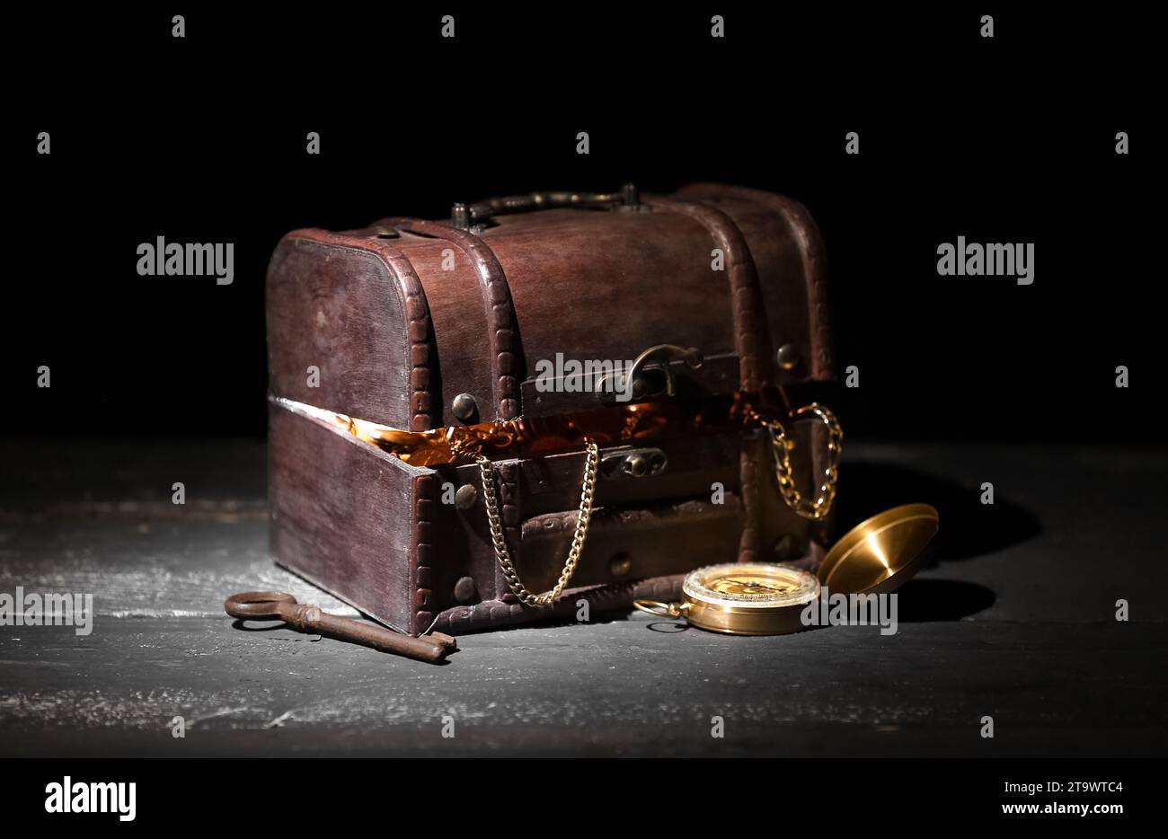 Old chest with treasures, key and compass on wooden table against black ...