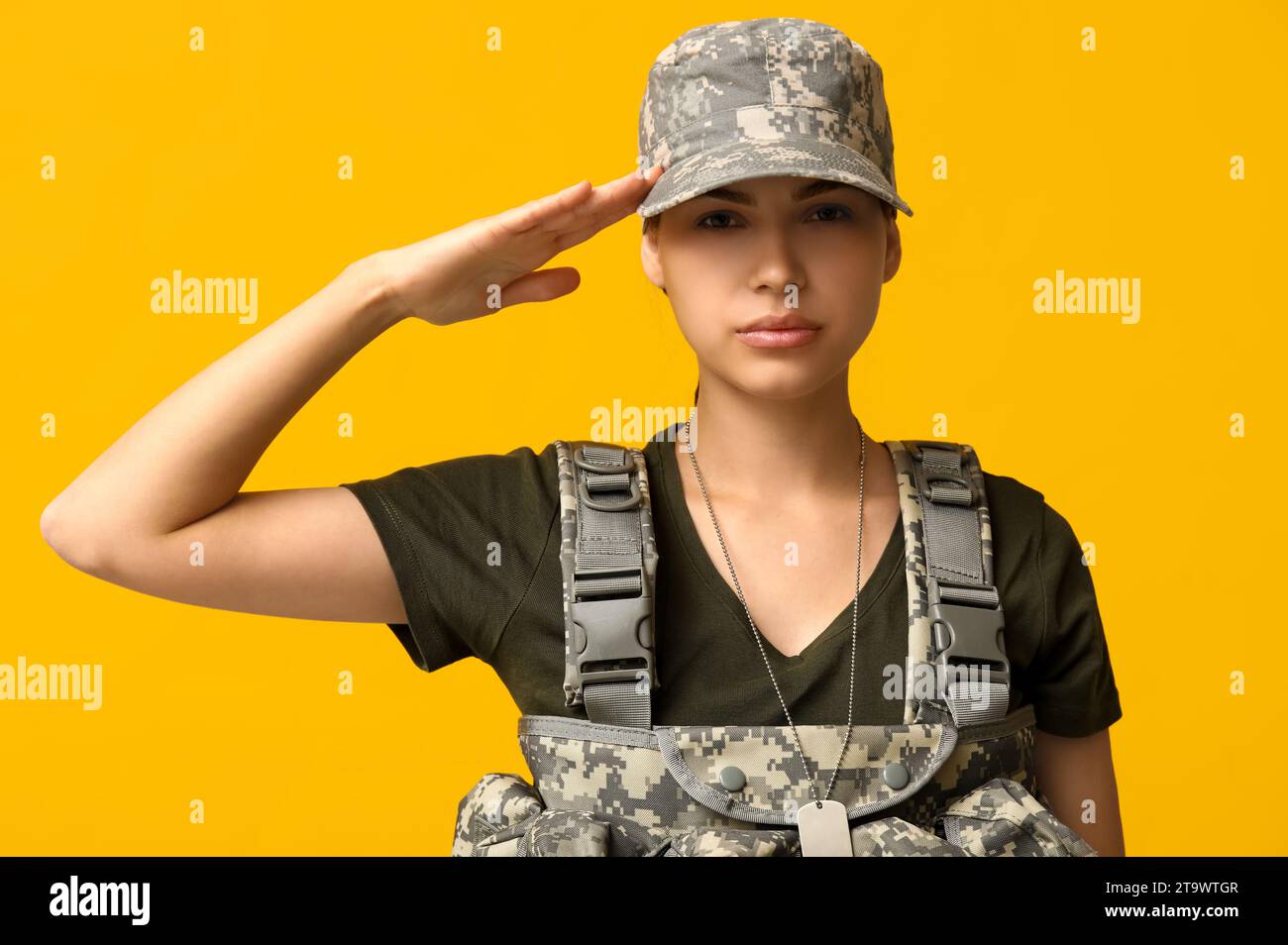 Confident young female soldier in uniform saluting on yellow background ...