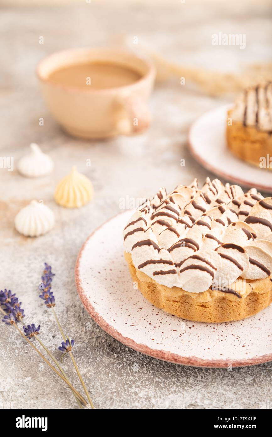 Two tartlets with meringue cream and cup of coffee on brown concrete ...