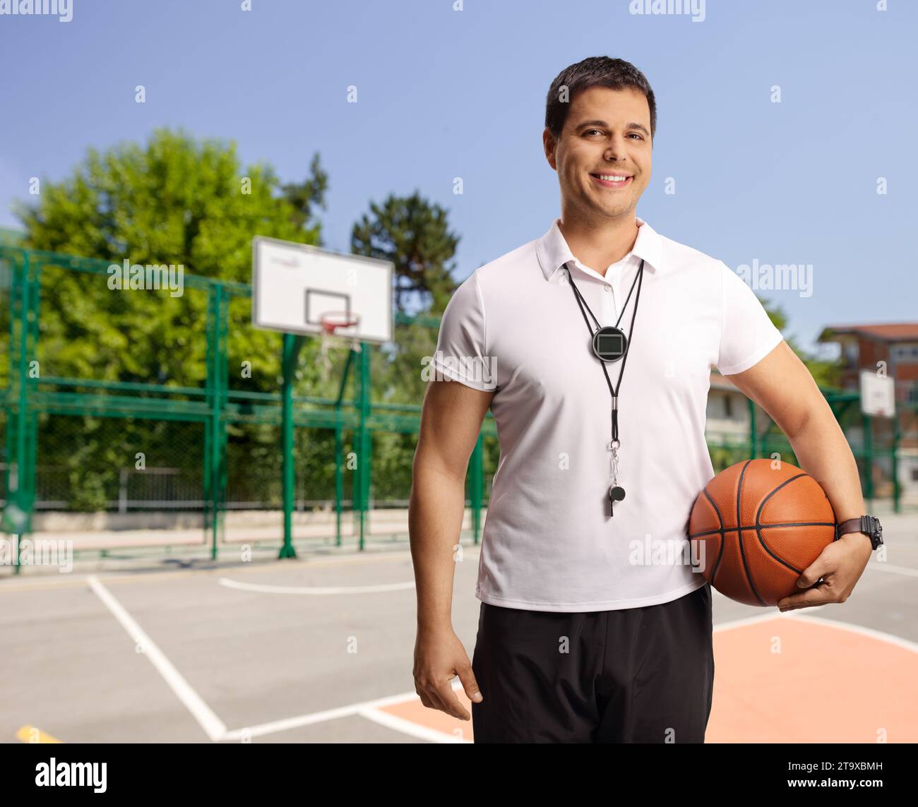 Coach holding a ball and posing on an outdoor basketball court Stock ...