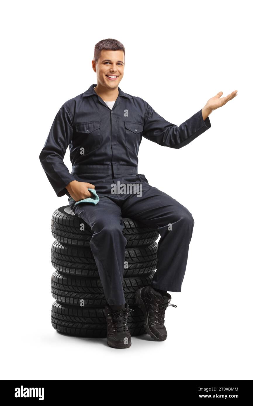 Auto mechanic worker sitting on a pile of tires and gesturing welcome ...