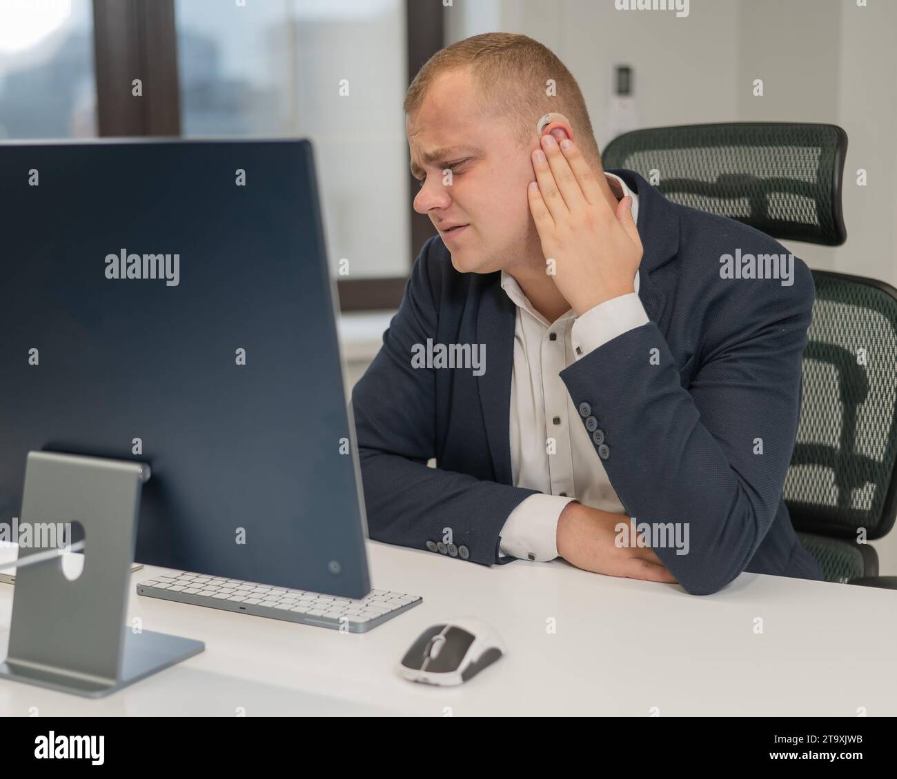 A deaf man works at a computer in the office. Broken hearing aid ...