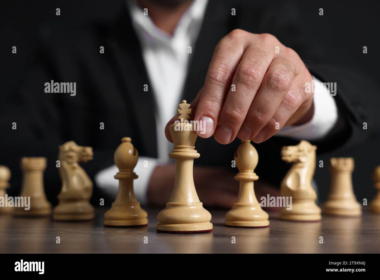 Man with chess pieces at wooden table against dark background, closeup ...