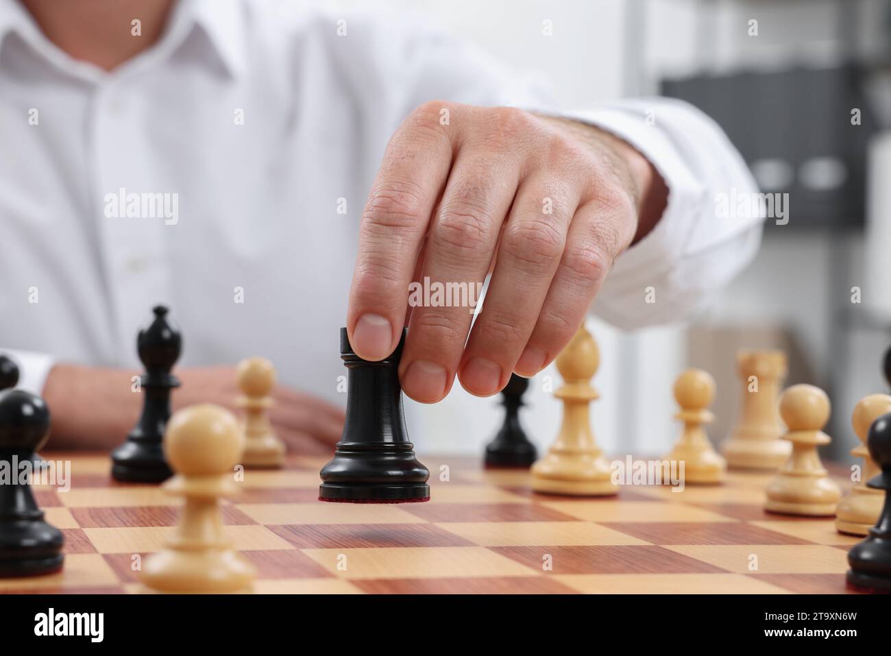 Man with rook game piece playing chess at checkerboard indoors, closeup ...