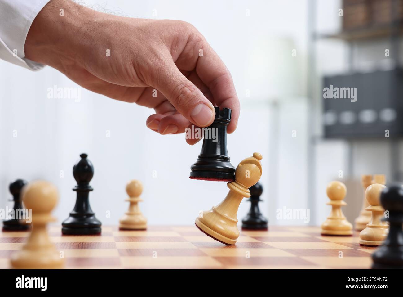 Man with rook game piece playing chess at checkerboard indoors, closeup ...