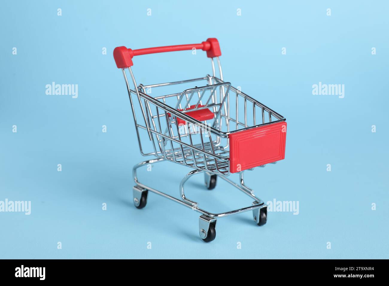 Small metal shopping cart on light blue background Stock Photo - Alamy