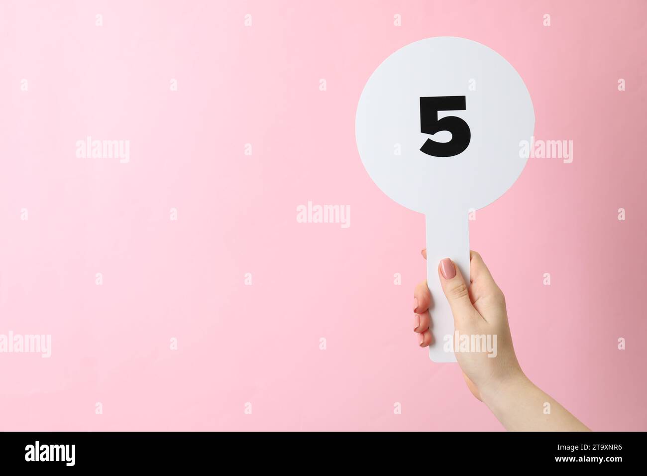 Woman holding auction paddle with number 5 on pink background, closeup ...