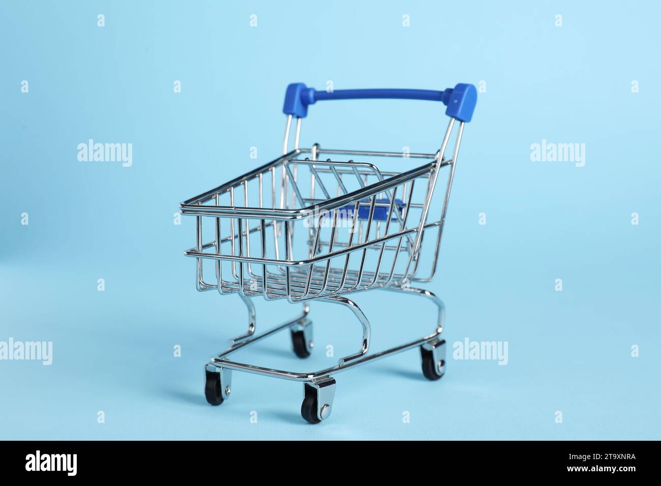 Small metal shopping cart on light blue background Stock Photo - Alamy