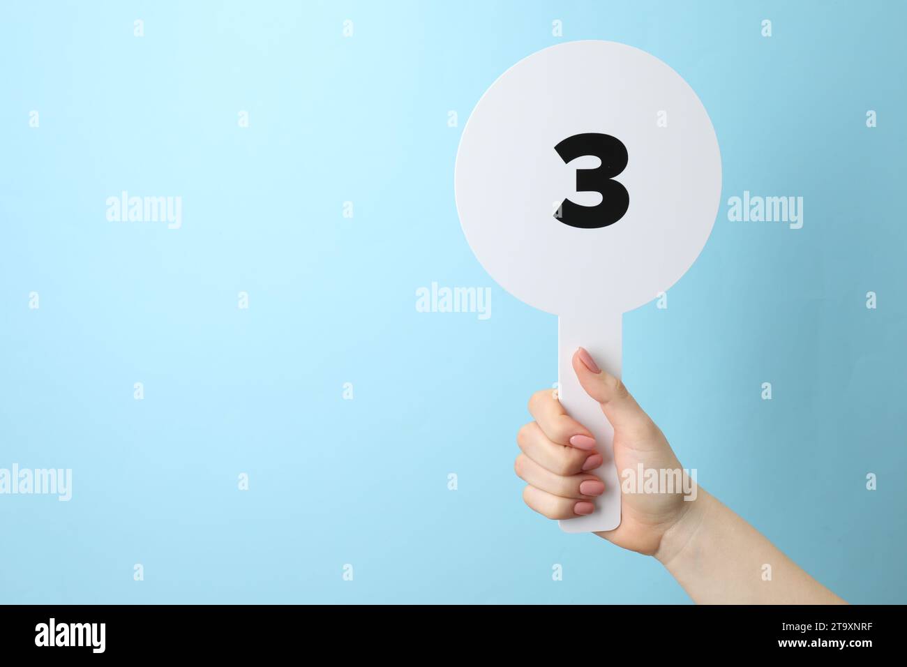 Woman holding auction paddle with number 3 on light blue background ...