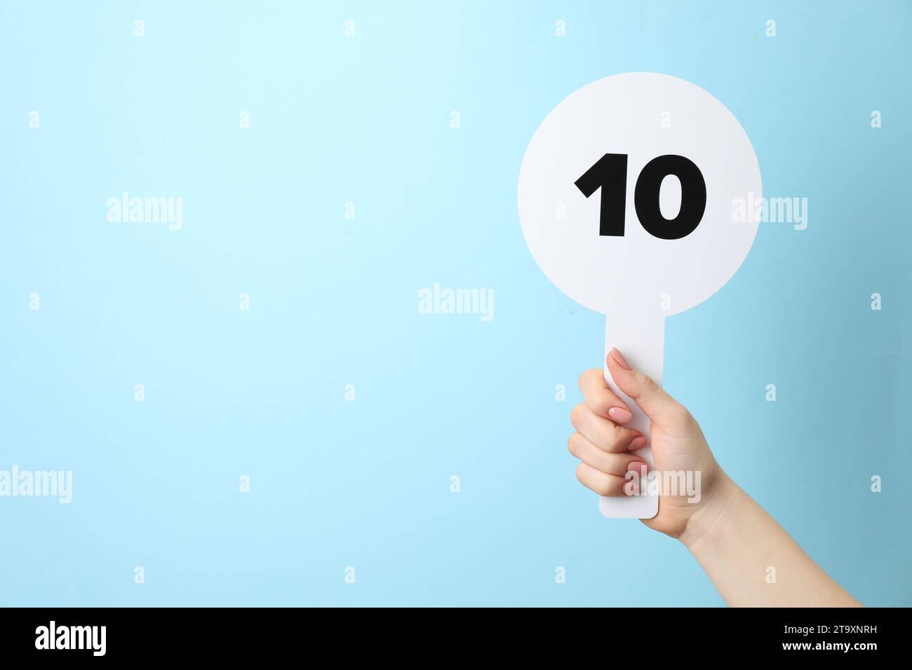 Woman holding auction paddle with number 10 on light blue background ...