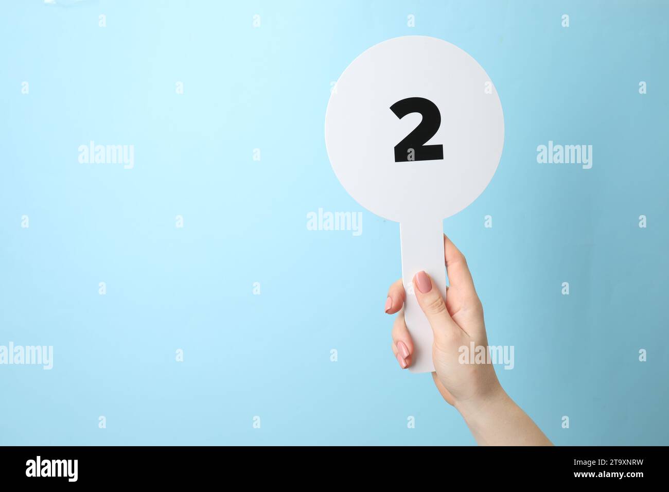 Woman holding auction paddle with number 2 on light blue background ...