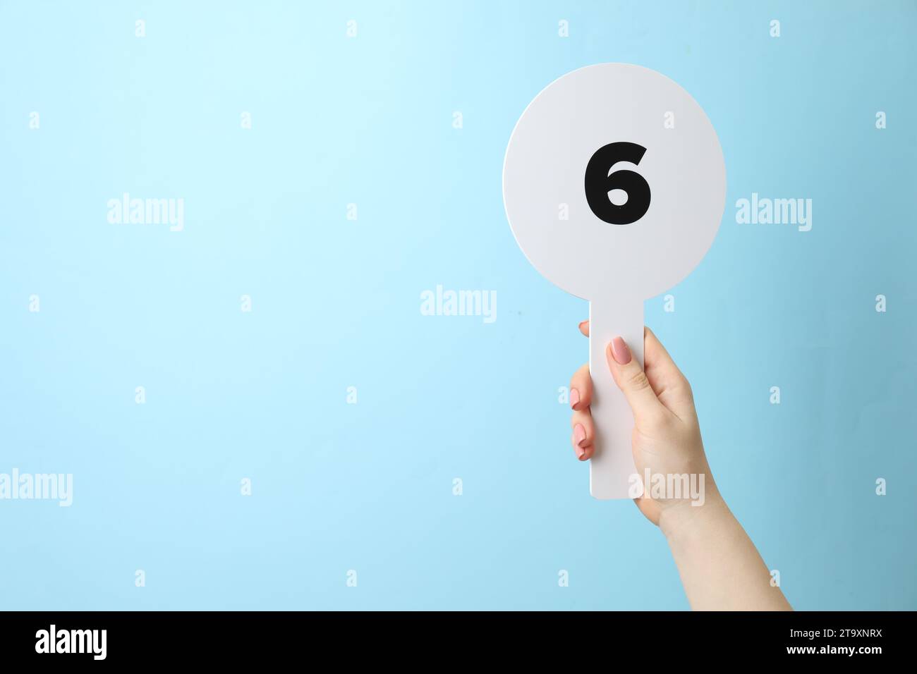 Woman holding auction paddle with number 6 on light blue background ...