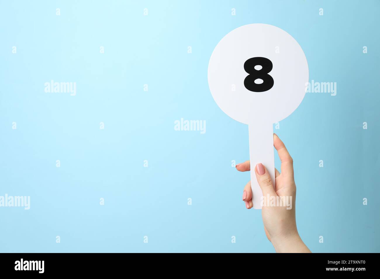 Woman holding auction paddle with number 8 on light blue background ...