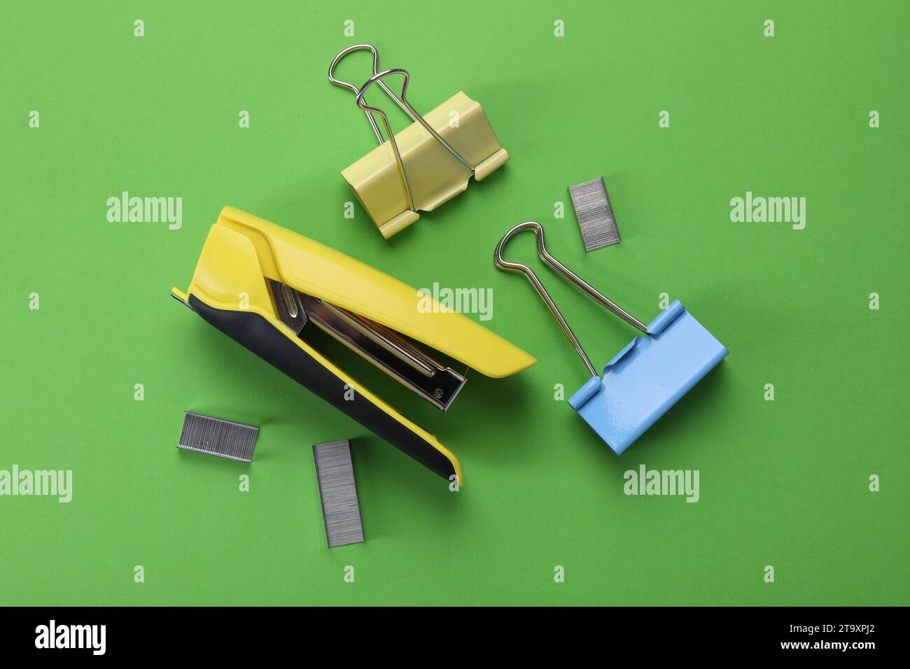 Yellow stapler with staples and binder clips on green background, flat ...
