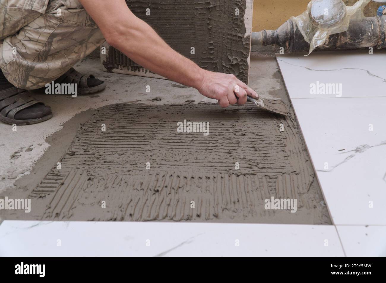 A construction worker applies cement for laying floor ceramic tiles ...