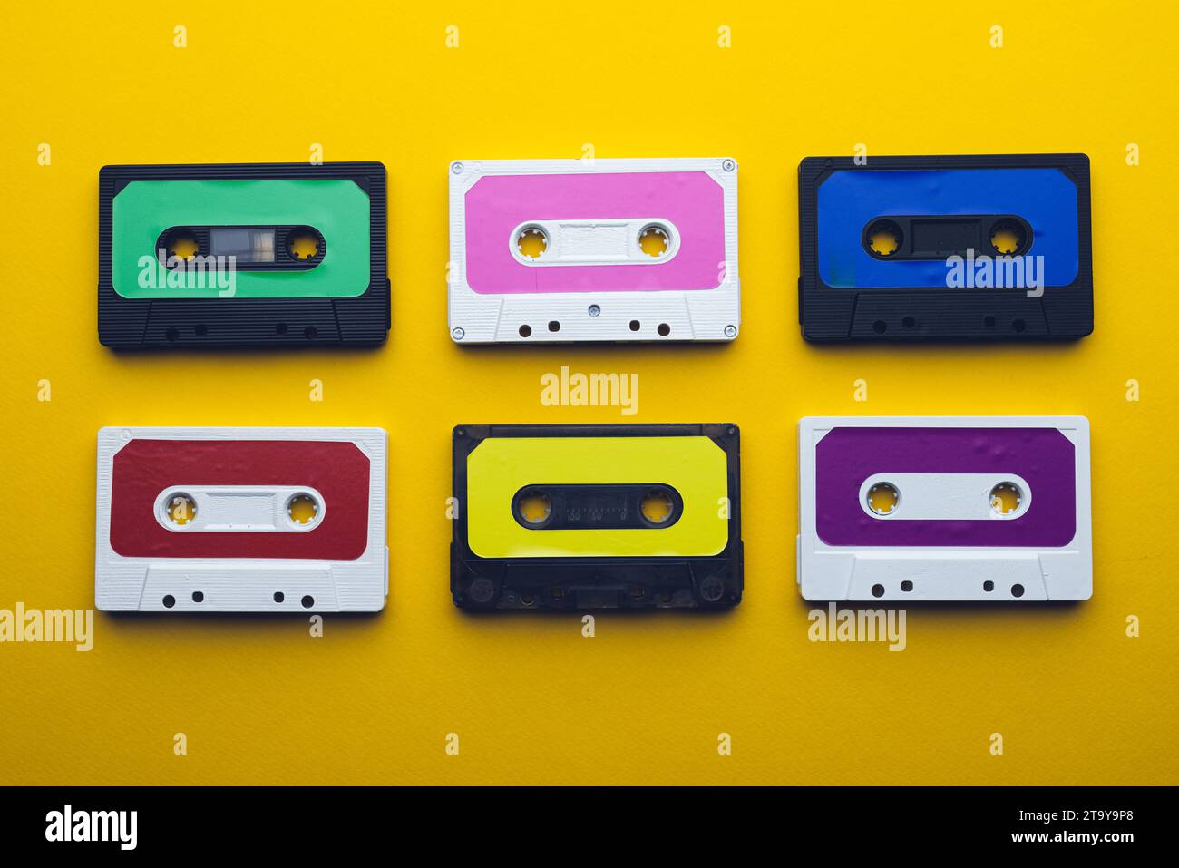 Overhead view of six colourful cassette tapes arranged on yellow ...